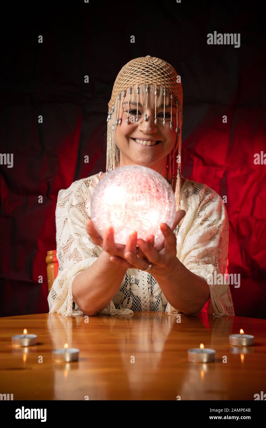 Fortune Teller with Crystal Ball on table with candles and black and ...