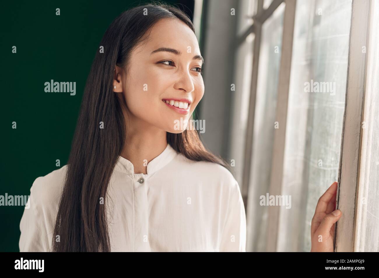 Freestyle. Young woman standing looking out the window smiling cheerful ...