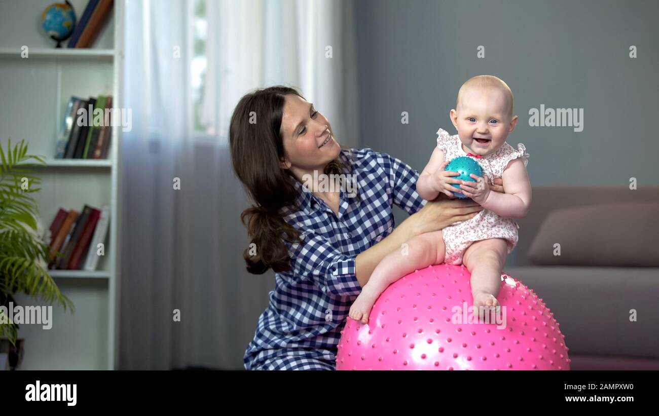 Responsible mother doing early development exercises with active baby ...