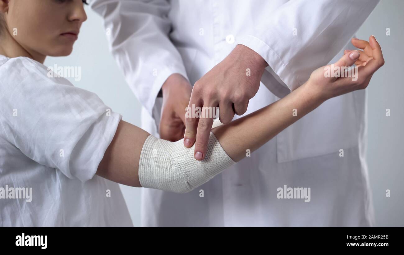Specialist taking care of injured elbow, bandaging, first aid in trauma ...
