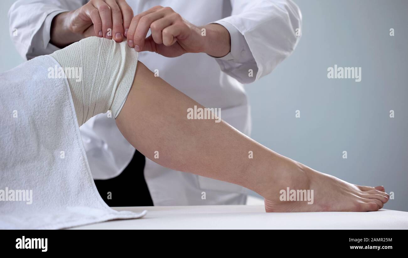 Traumatologist bandaging patients sprained knee, first aid for injuries ...