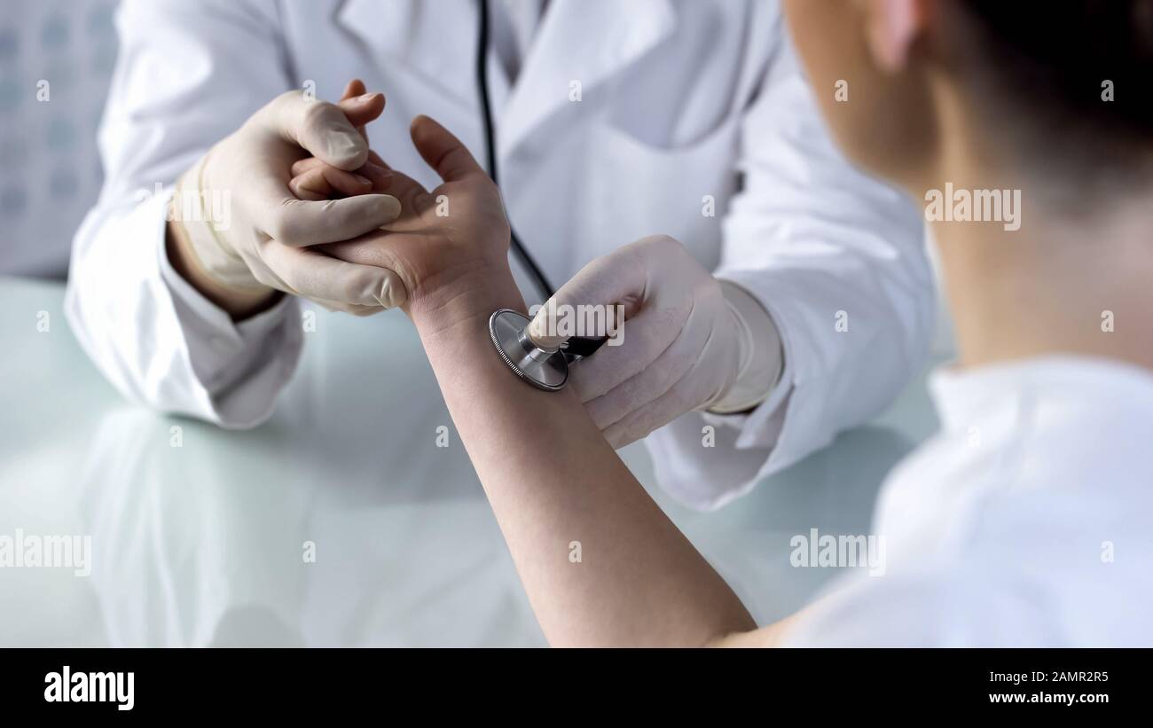 Physician examining females pulse with stethoscope, hospital ...