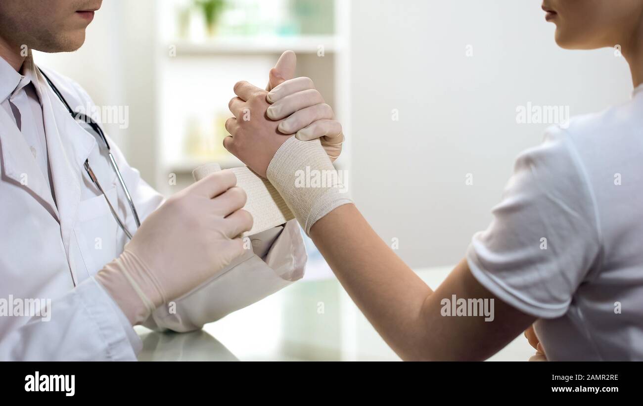 Male physician bandaging females sprained wrist, first aid in hospital ...
