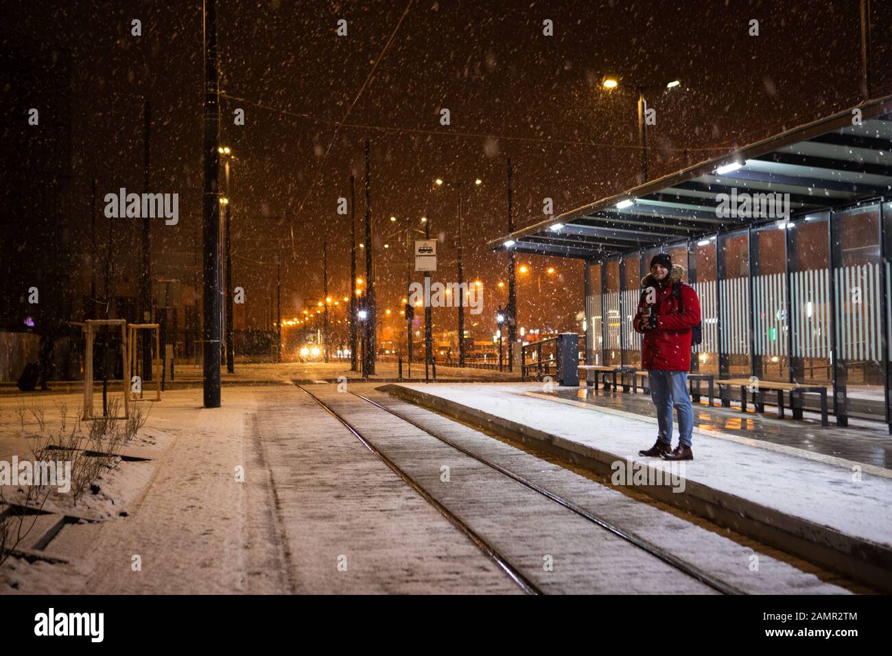 man in red winter coat standing at bus tram stop waiting for public ...