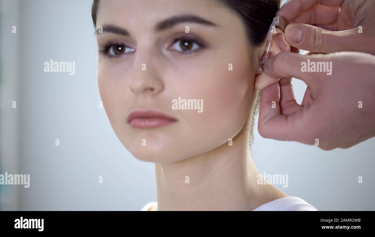 Doctor puts deaf aid on young ladys ear, hearing impairment, work for ...