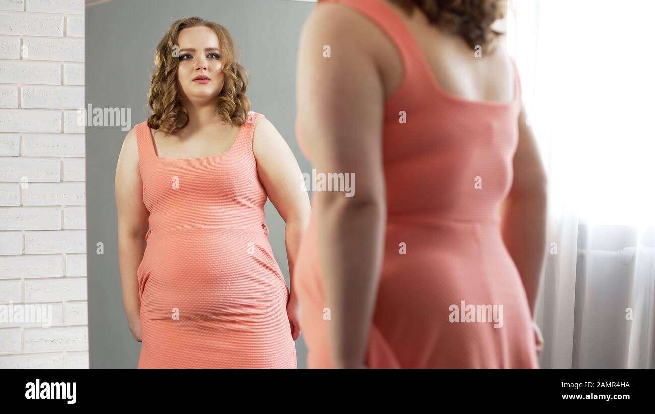 Plus-size female looking in mirror, upset about her weight, suffer ...