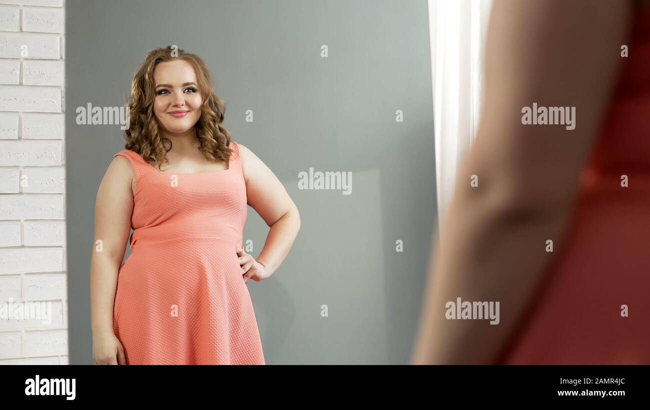 Plump lady looking in mirror with charming smile, self-confidence, body ...