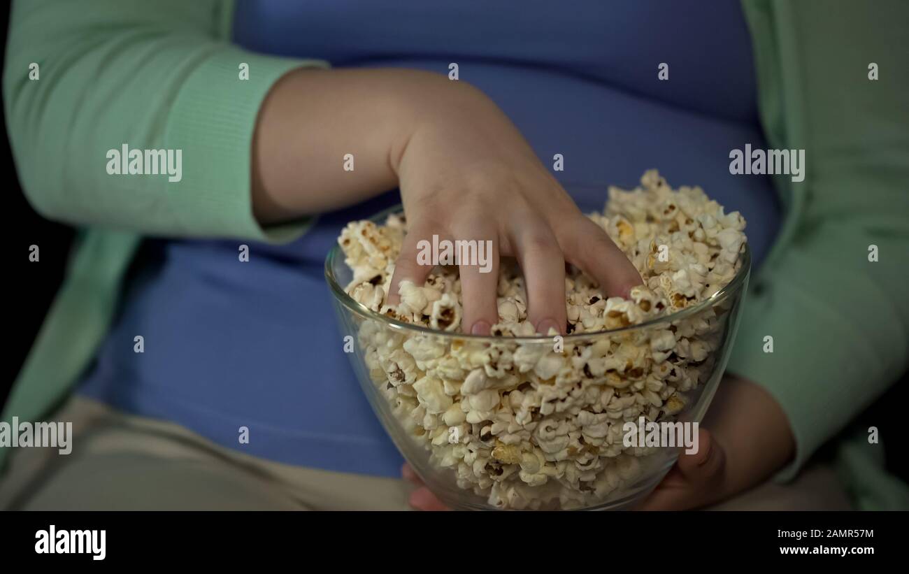 Chubby woman taking handful of fatty popcorn, sedentary lifestyle ...