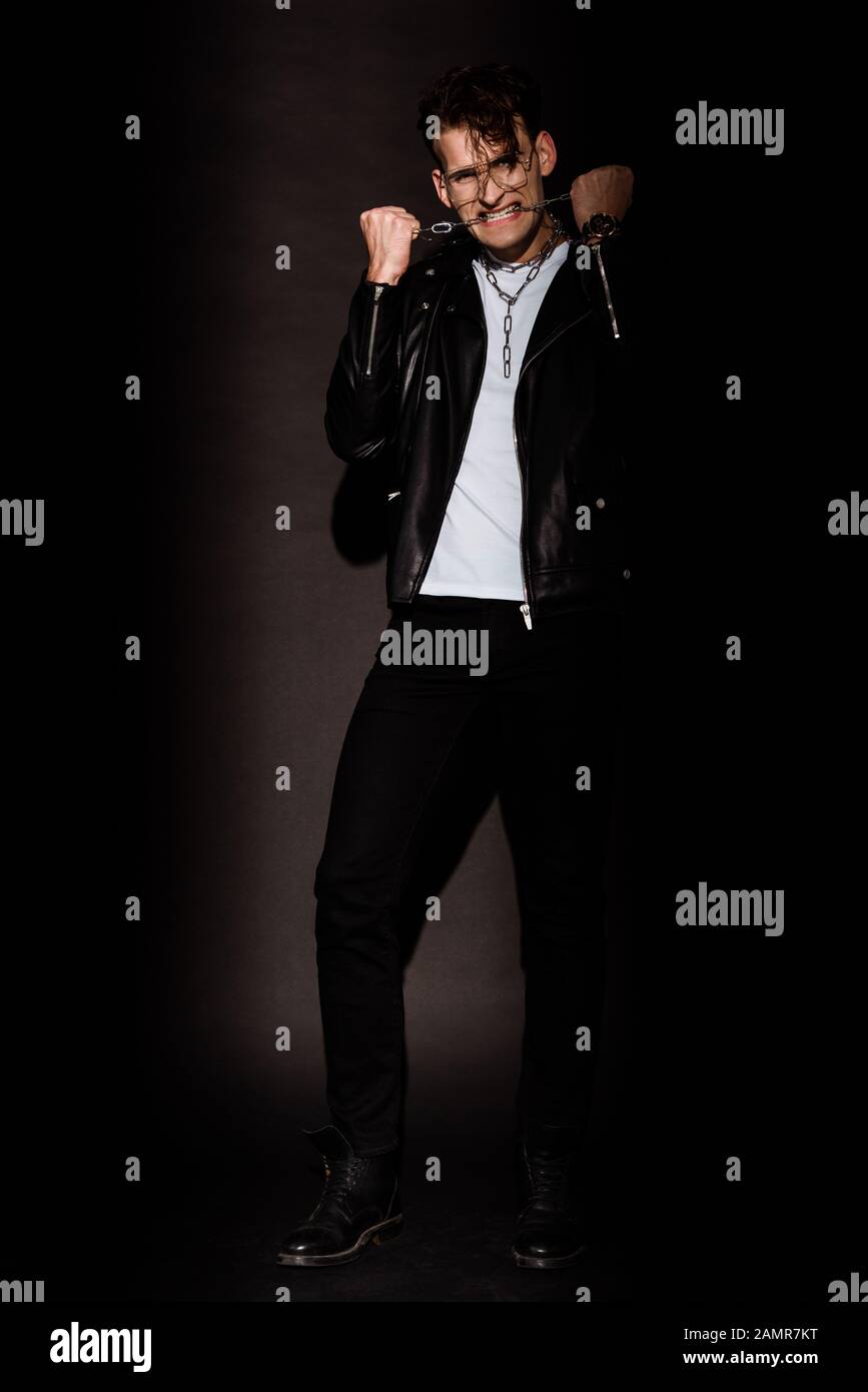emotional man biting metallic chains and standing on black Stock Photo ...