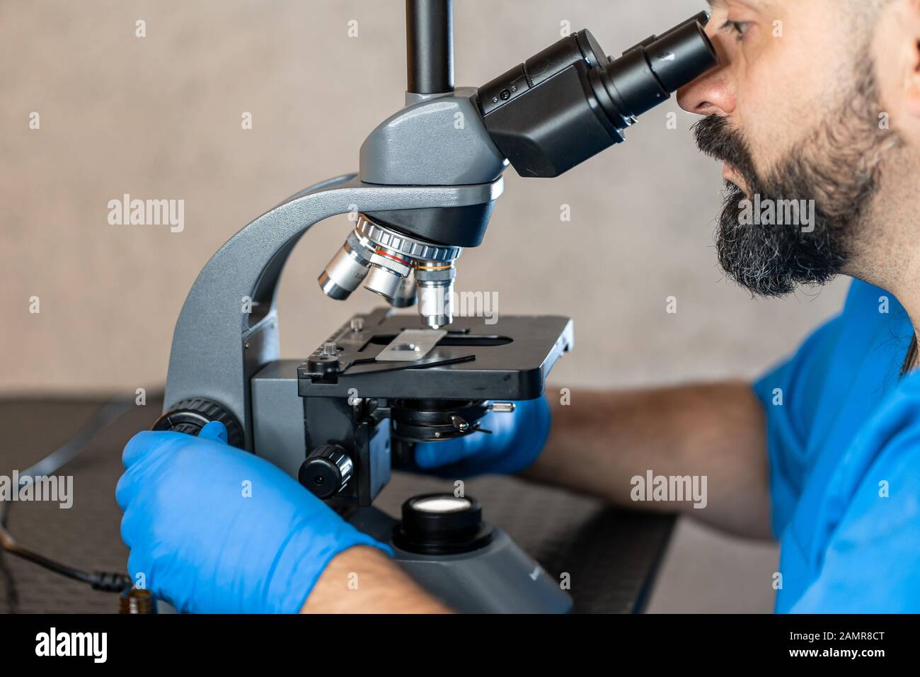 Male laboratory assistant examining biomaterial samples in a microscope ...