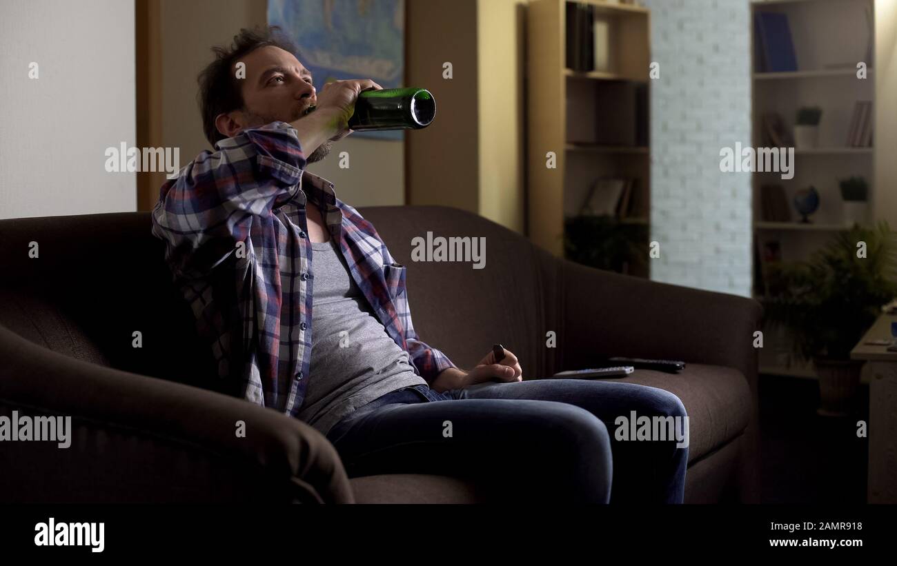 Lazy male drinking bottled beer with pleasure, sitting on sofa ...