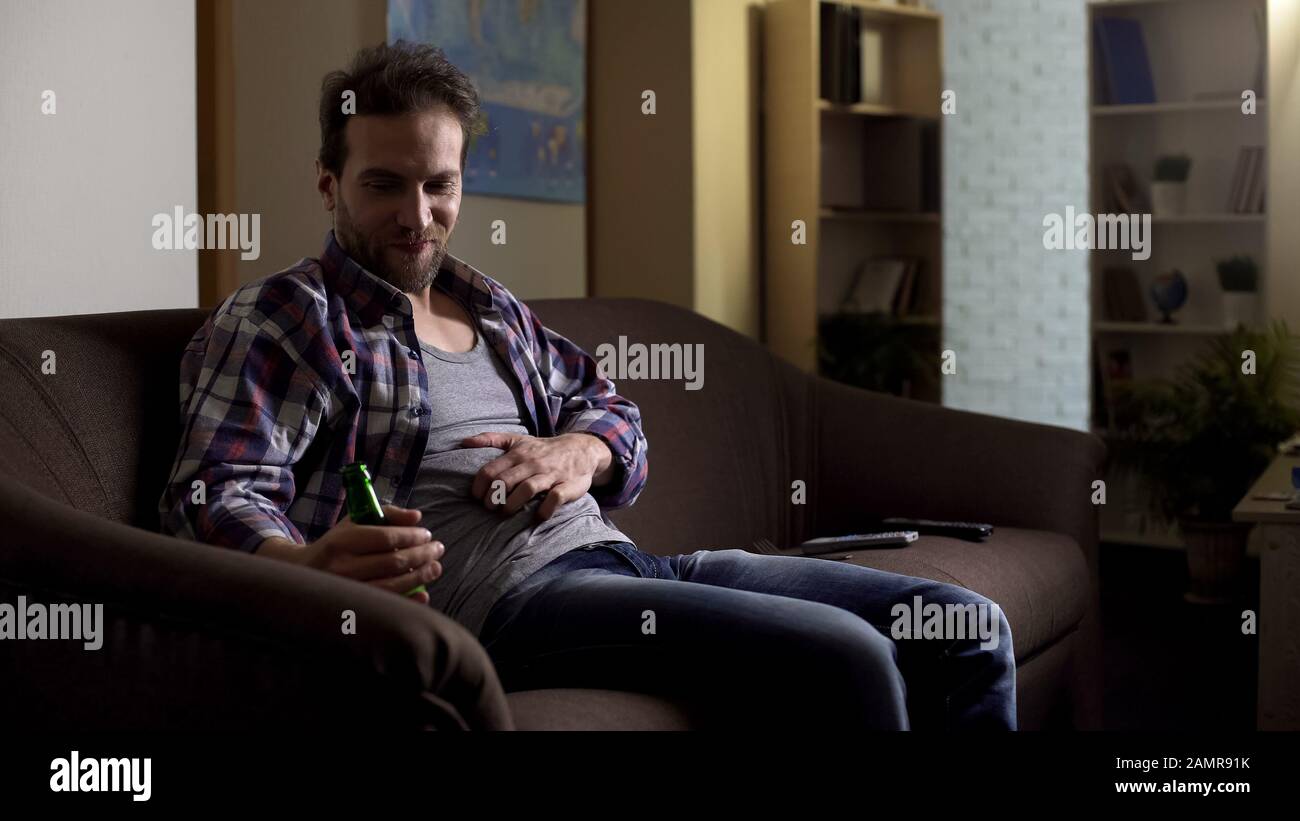Untidy man drinking beer with content, rubbing belly, addiction to ...