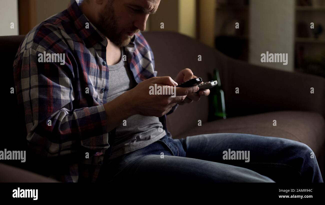 Guy sitting on couch, using remote control for TV set, getting angry ...