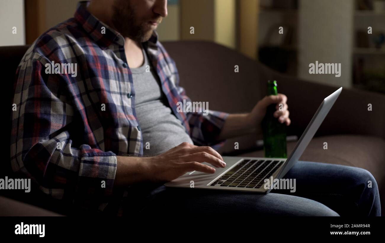 Untidy man on sofa using laptop and drinking beer, browsing internet ...