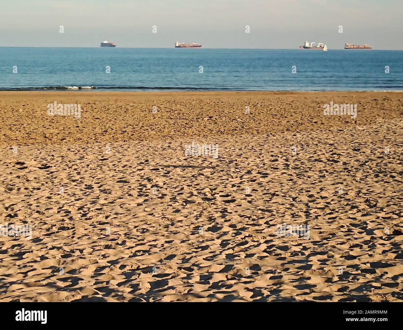 Beach sand at sunset with cargo ships sailing in the sea in the ...