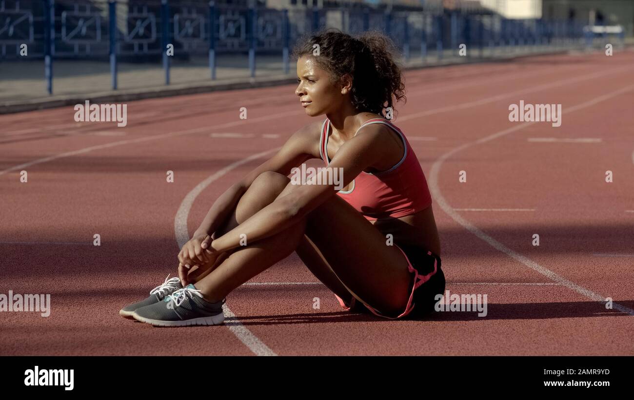 Cute athletic girl tired after workout at stadium sitting on track ...