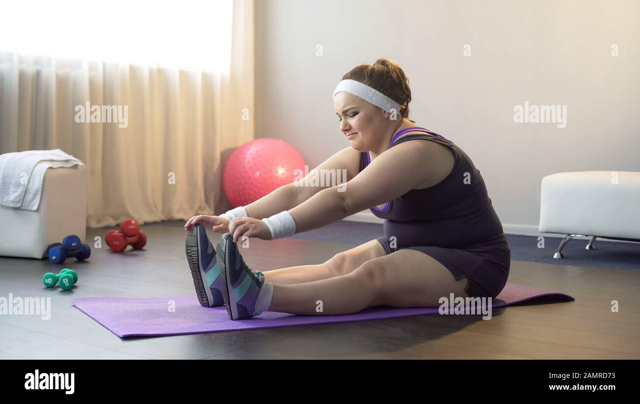 Tired overweight girl trying to reach toes with great effort ...