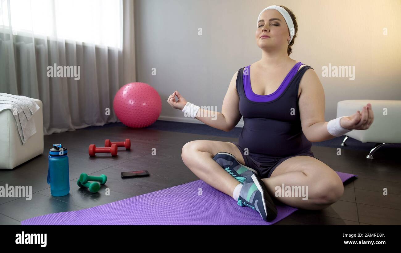 Plus-size lady sitting in lotus position, meditating and breathing ...