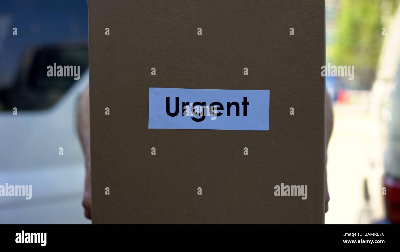 Urgent delivery courier in uniform holding cardboard box, international ...