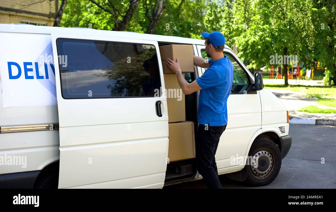 Male delivery worker taking cardboard box from van, parcel shipment ...