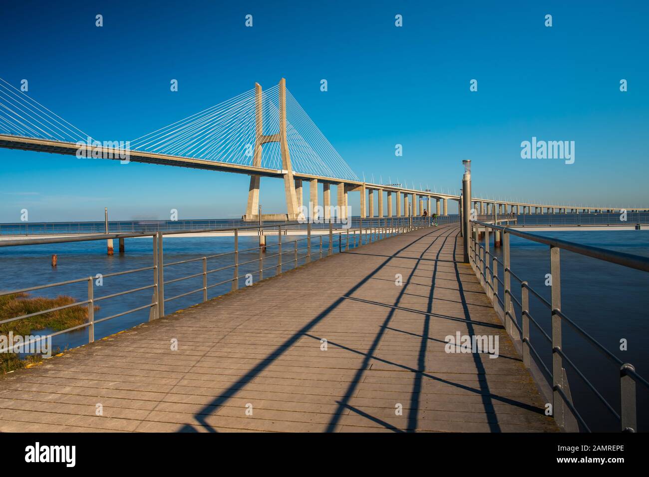 Long wooden pier leading toward a modern cable-stayed bridge under a ...