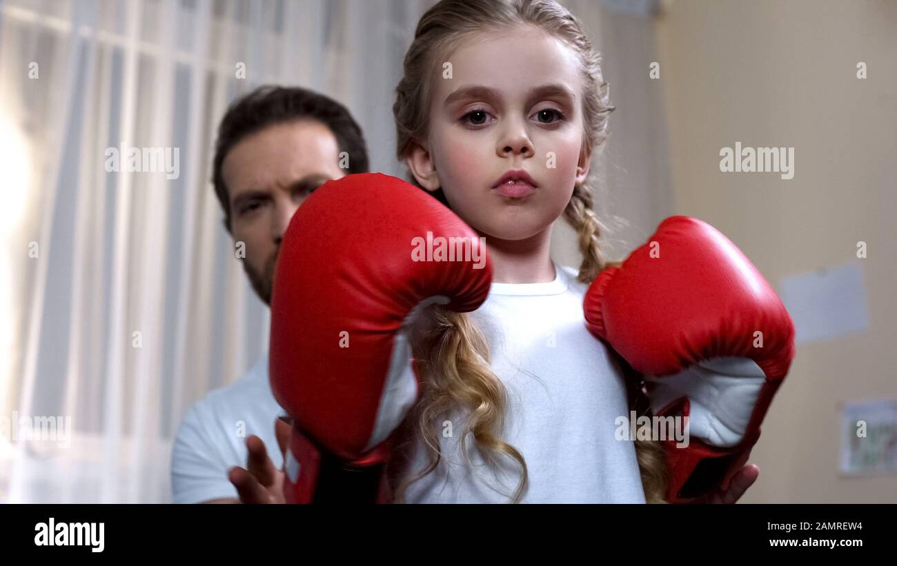Pretty kid in boxing gloves practicing punches with father behind ...