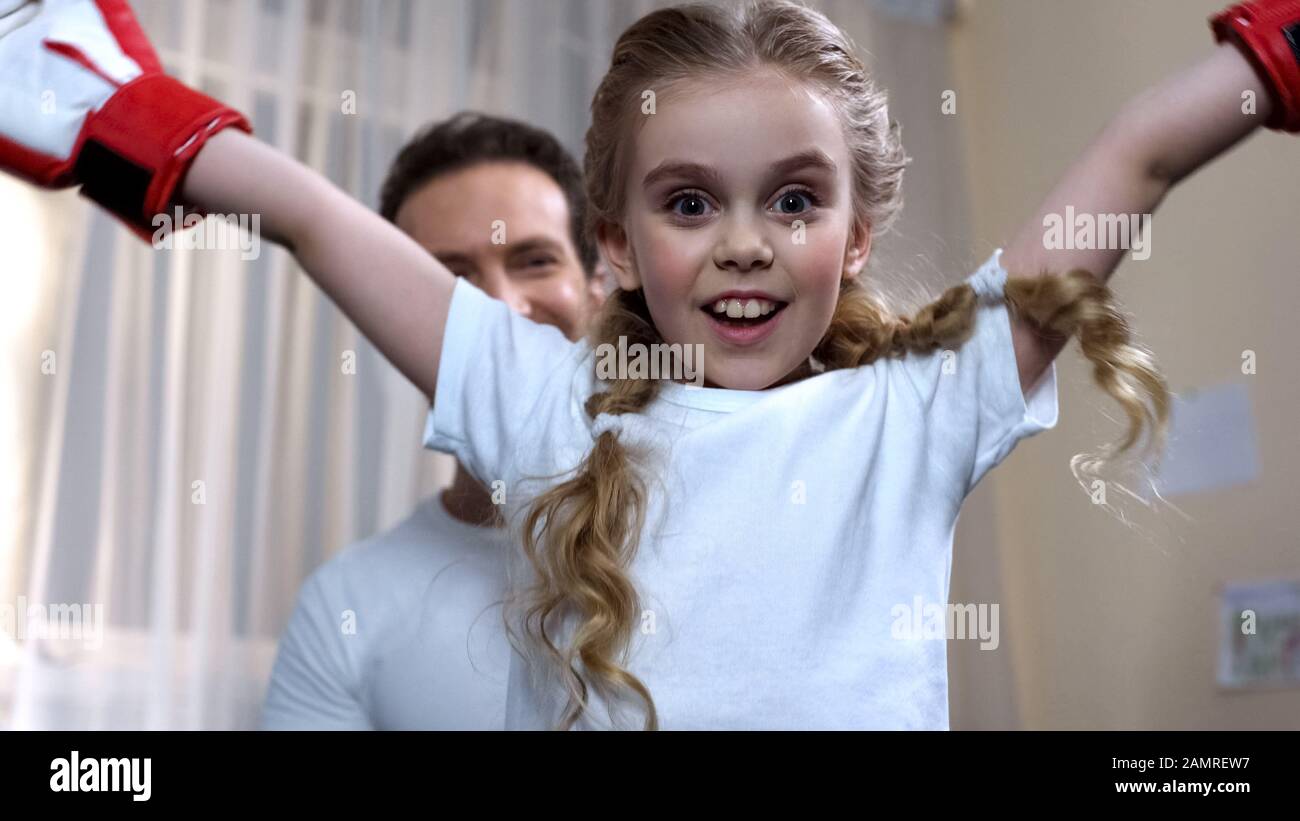 Little girl in boxing gloves showing yes gesture, father behind her ...