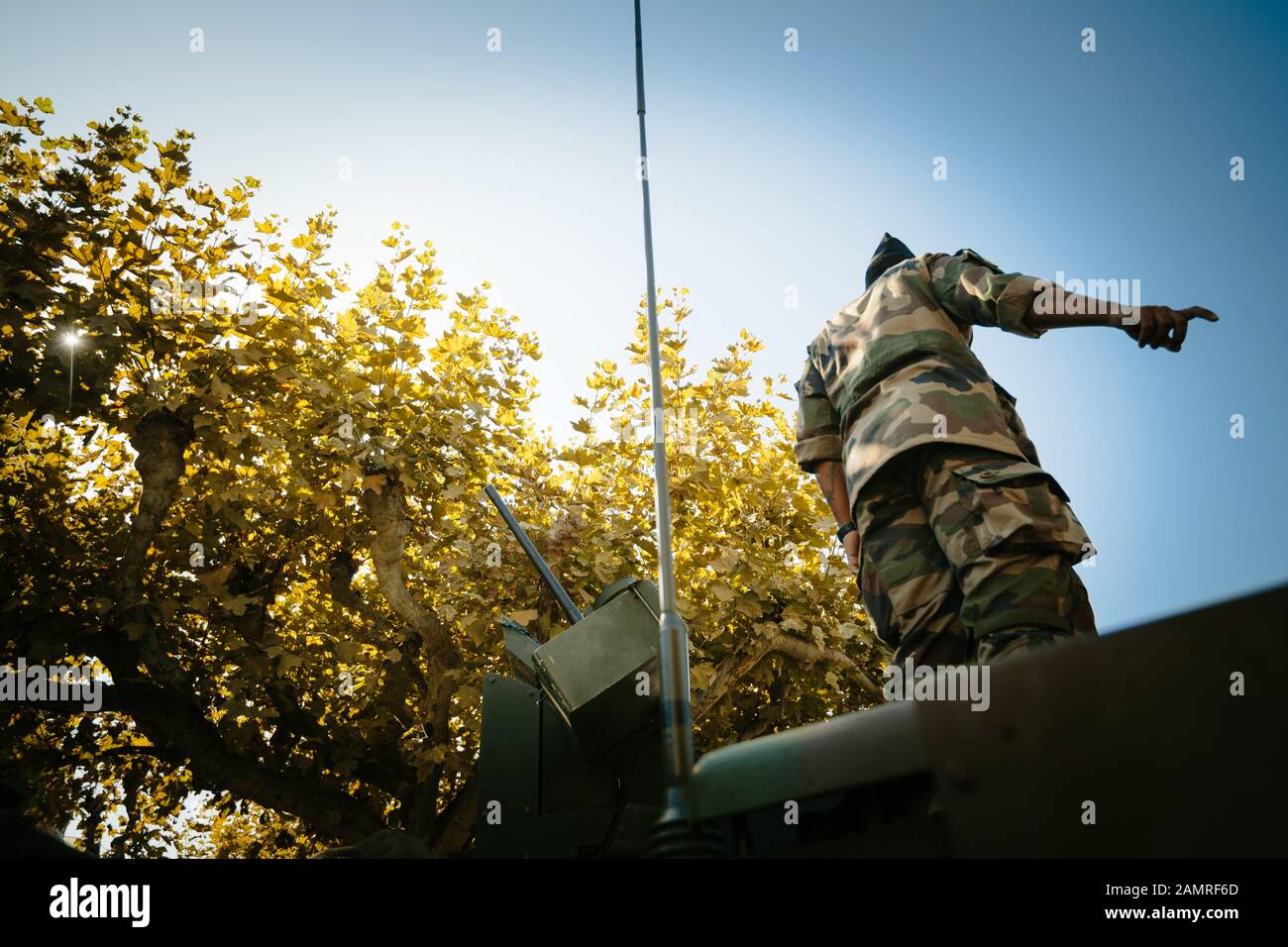Low angle rear view of solider on top of military vehicle giving ...