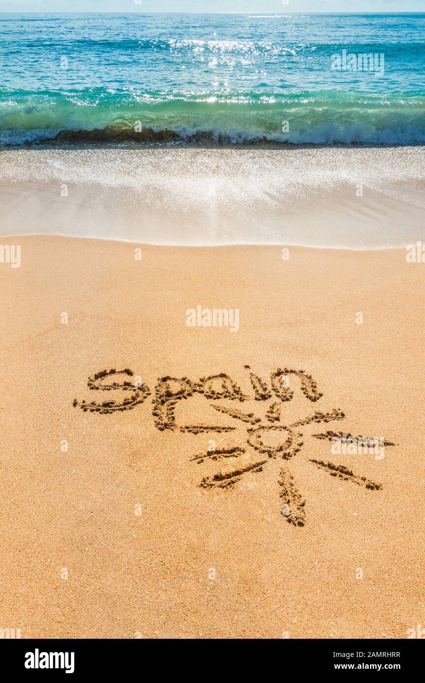 Hand written text Spain and sun symbol on the golden beach sand with ...