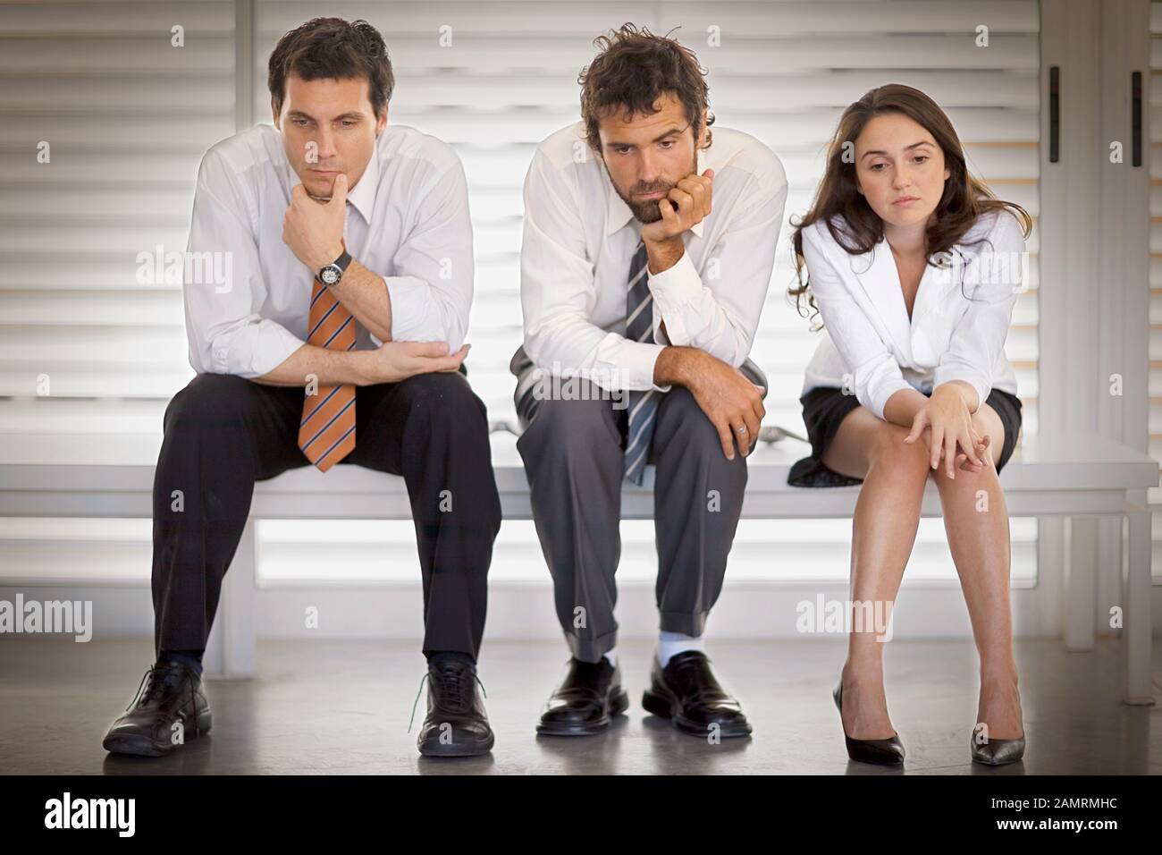 Three bored business colleagues sitting side by side on a bench inside ...