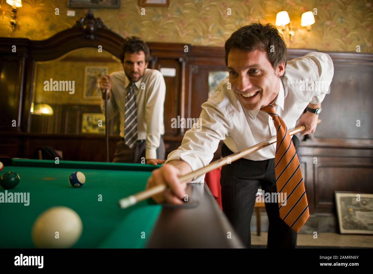 Happy young businessman lining up a ball with his cue during a game of ...