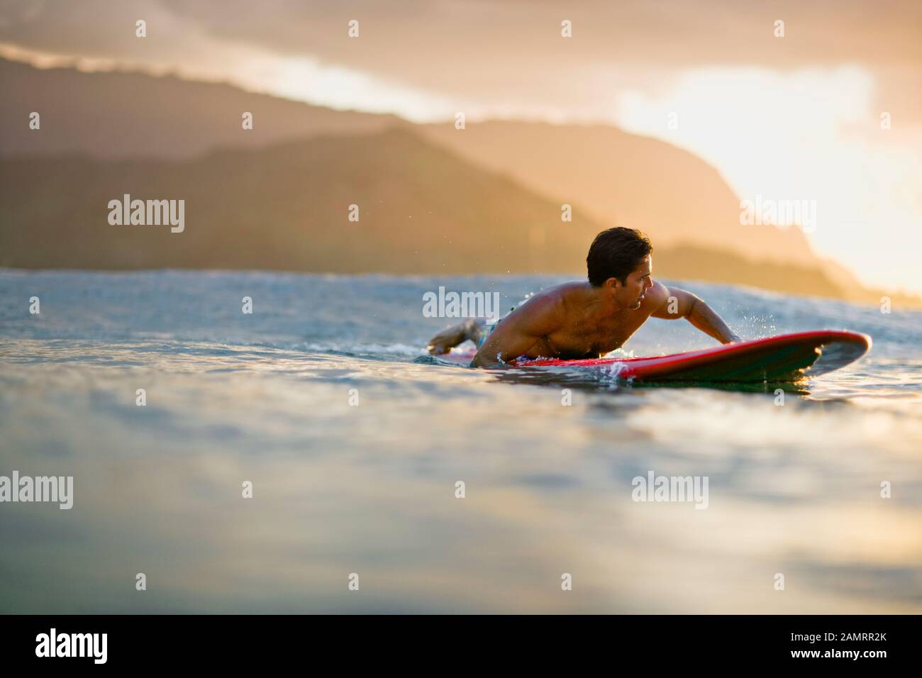 Male surfer lies on his board, looks over his shoulder and paddles in ...