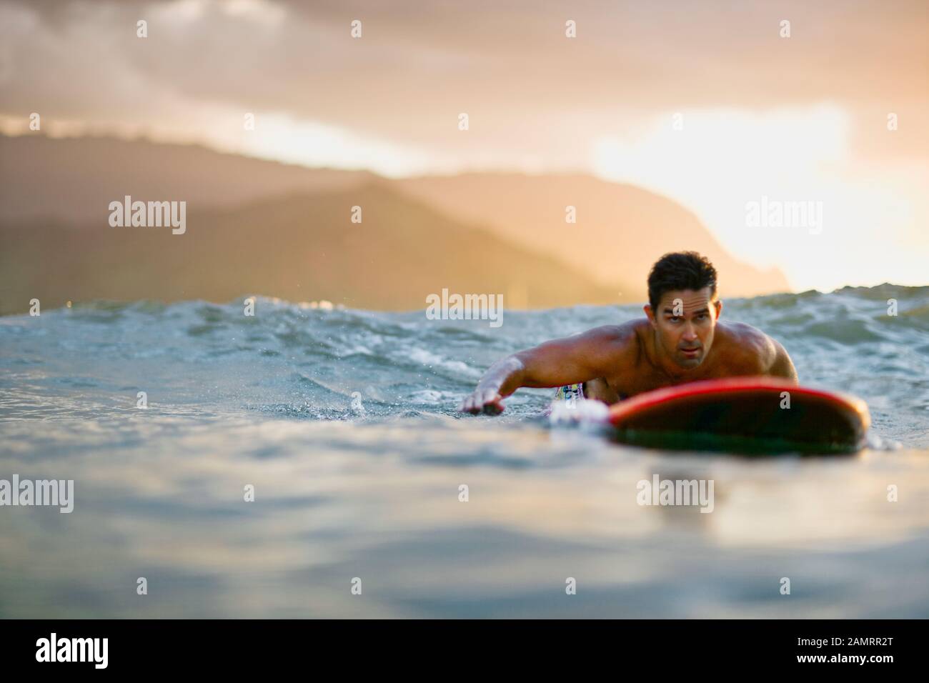 Male surfer lies on his board, looks forward and paddles in ...
