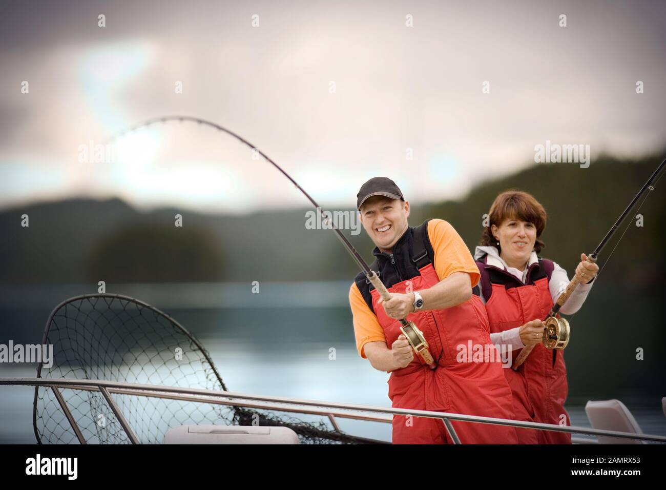 Smiling mid adult man fishing while standing on the deck of a boat with ...