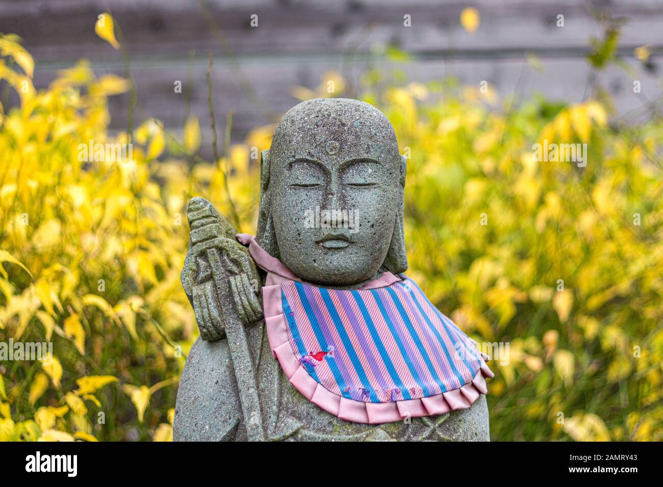 Buddhist stone relic with purple bib and holding symbolic staff ...