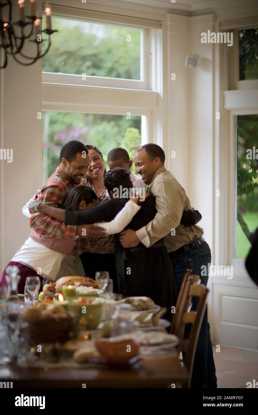 Family smiling and hugging by the dinner table Stock Photo - Alamy