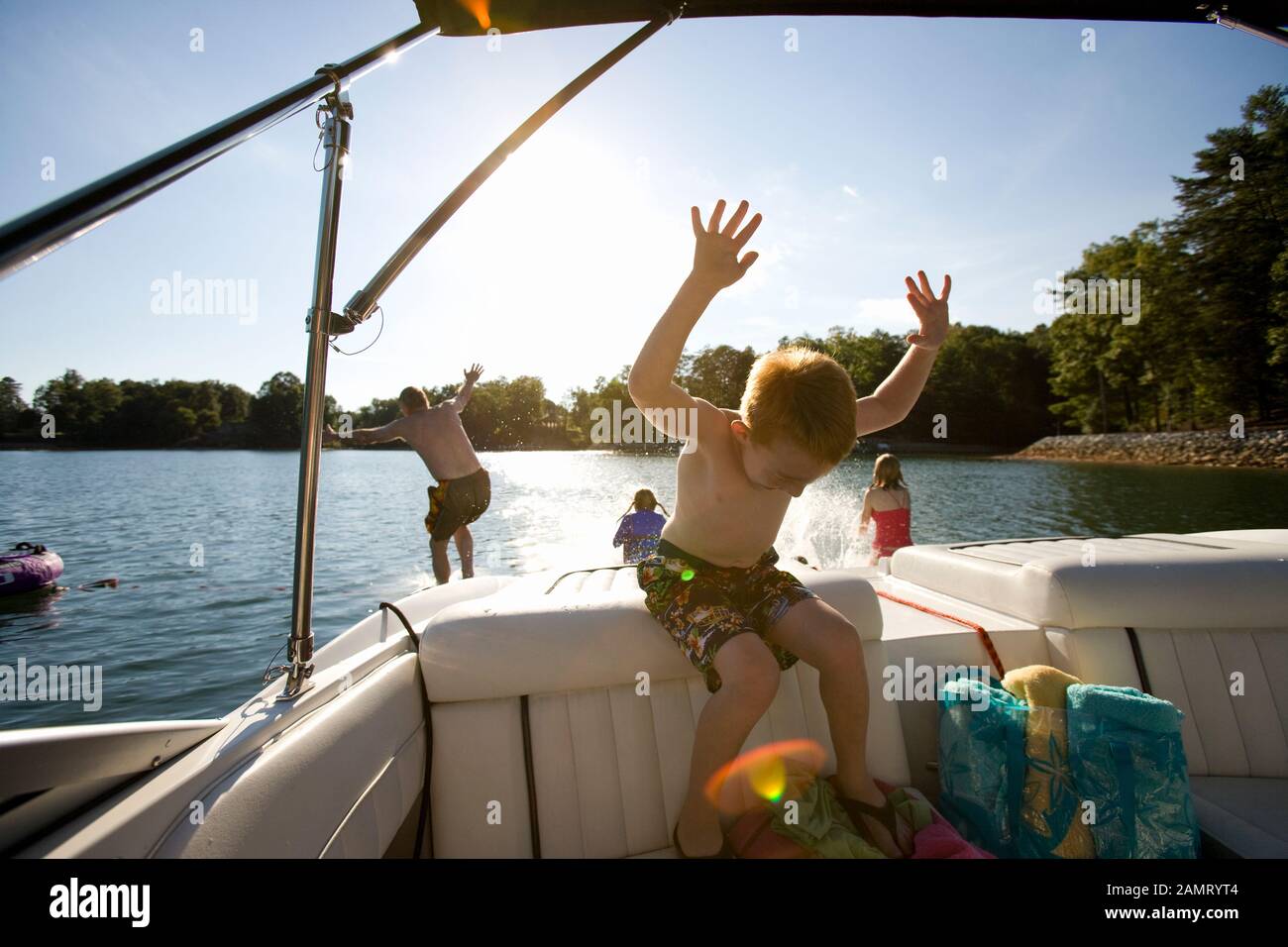 Young boy sitting on a boat with his hands up as his family jump into ...