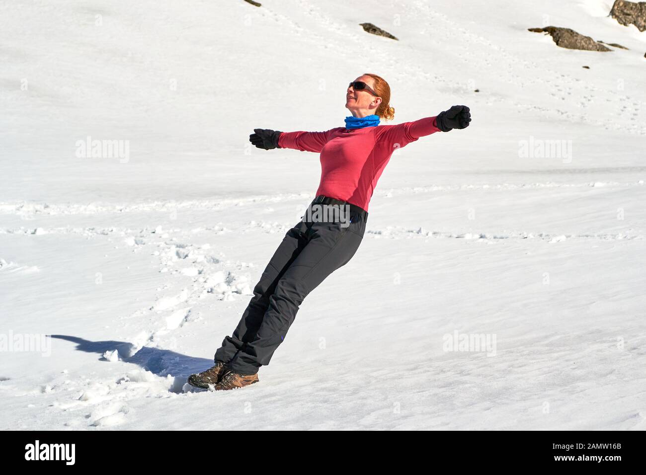 Woman letting herself fall on her back in snow with her arms spread out ...