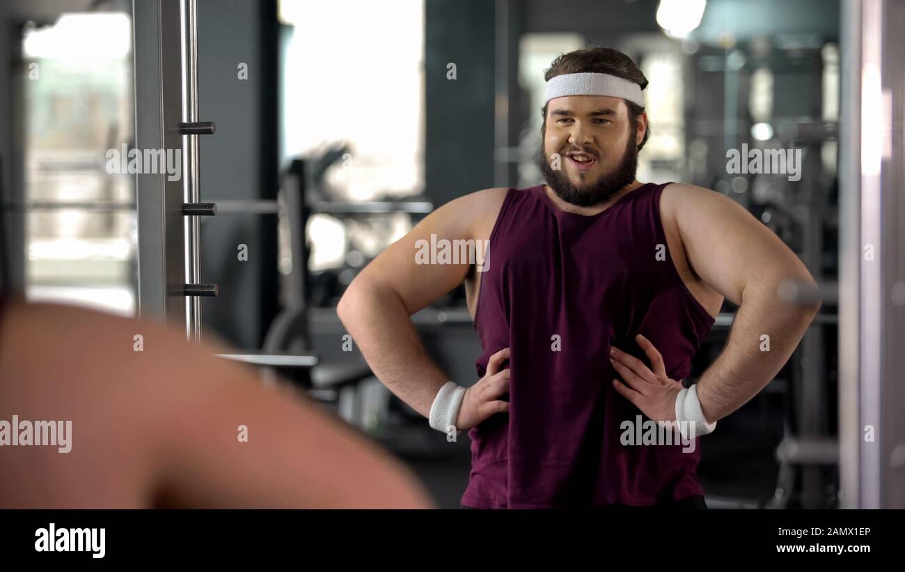 Funny obese man looking at mirror reflection and posing like macho ...