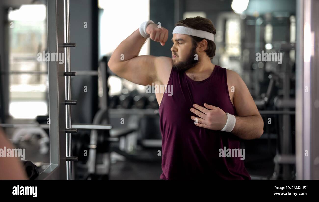 Funny fat man looking at mirror reflection gym and posing, pretending ...