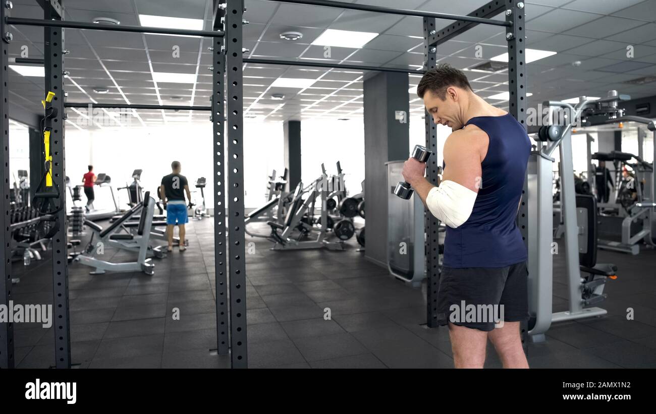Strong man with injured elbow training with dumbbell in gym, recovery ...