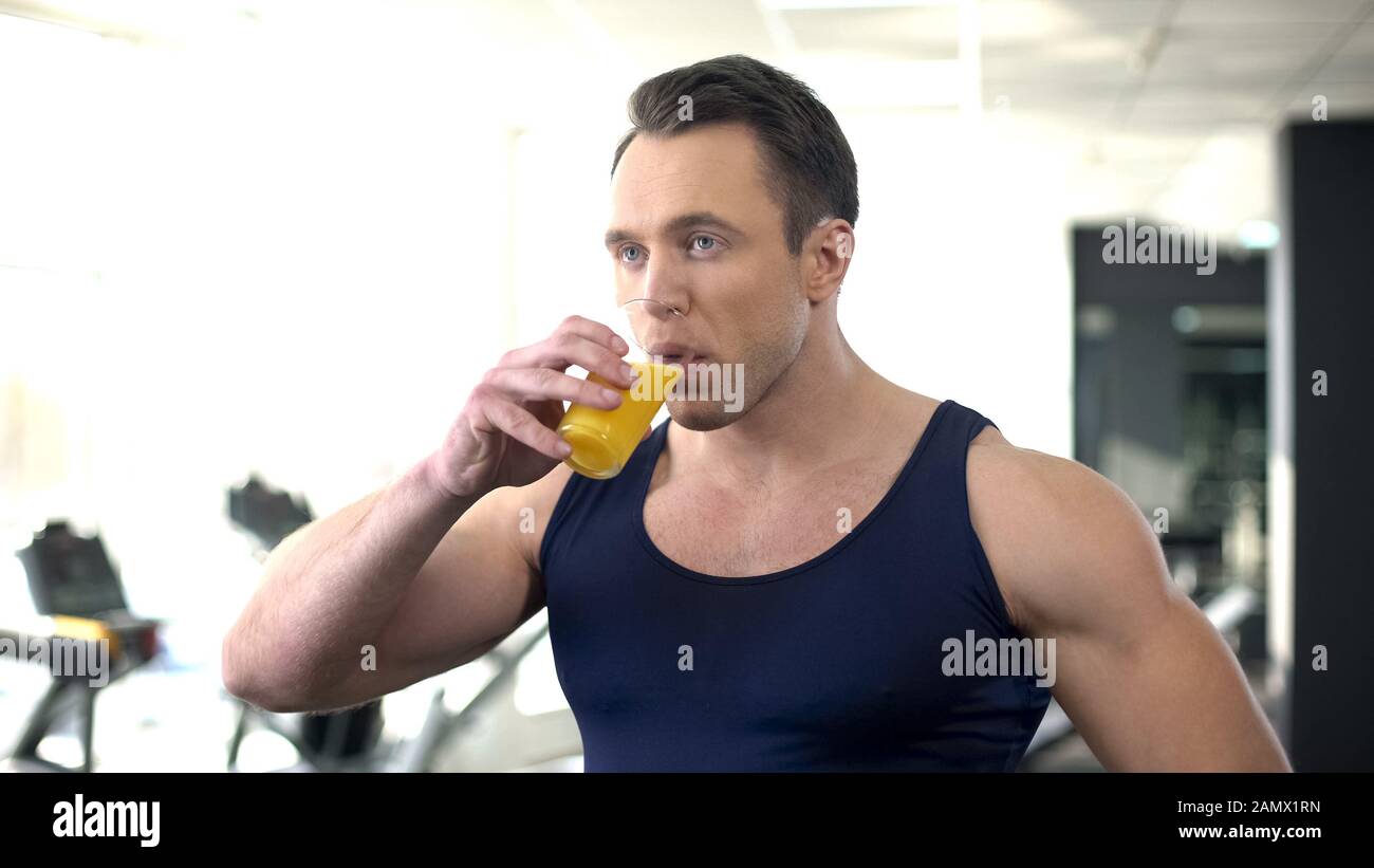 Bodybuilder drinking fresh orange juice, balanced fitness nutrition ...