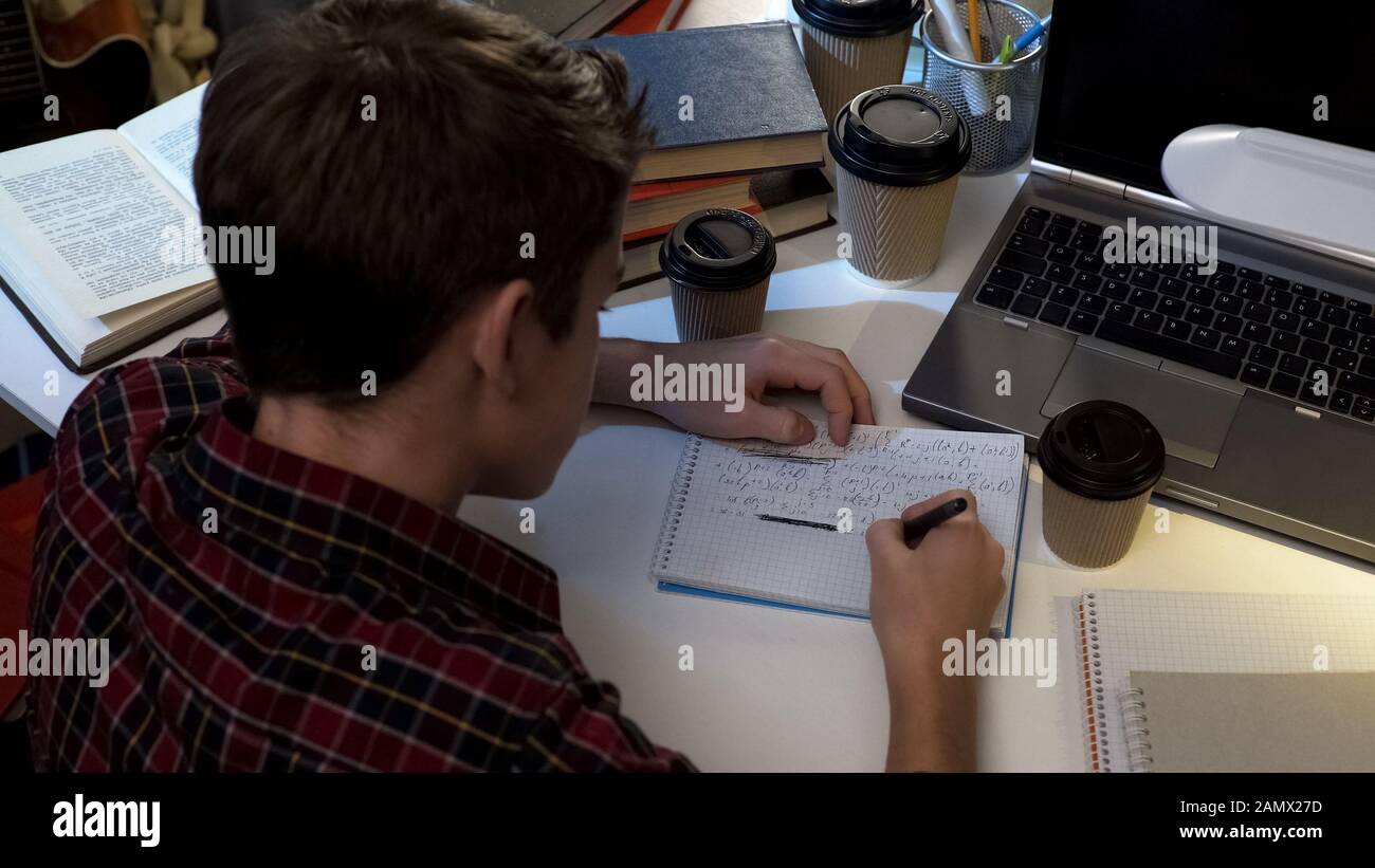 Teen boy student doing math and drinking energetic beverages in evening ...