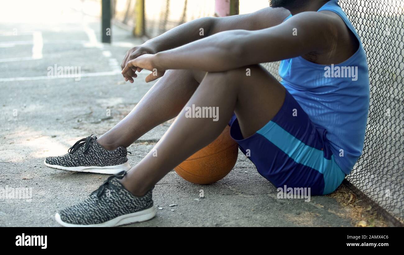 Sad Afro-American basketball player sitting on ground, lack of ...