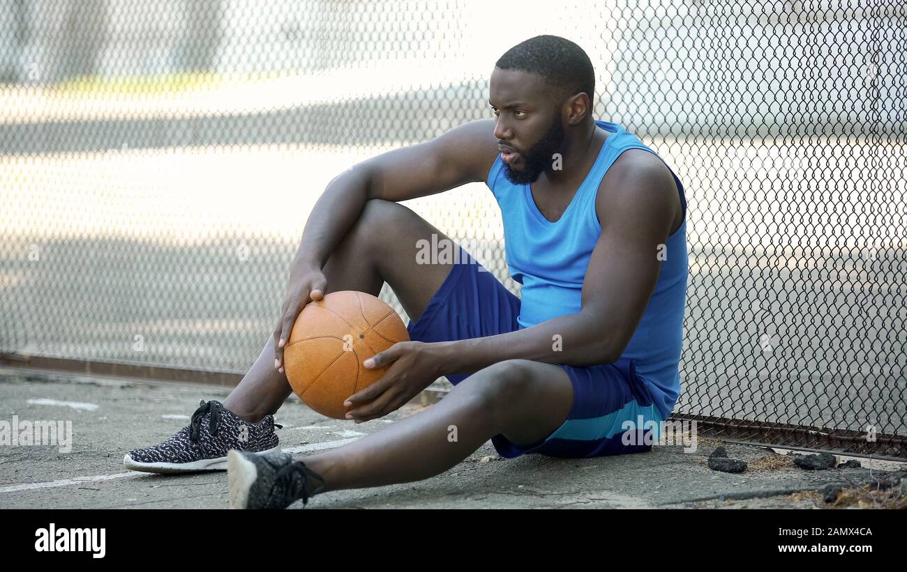 Nervous man in sportswear sitting alone near stadium and holding ball ...