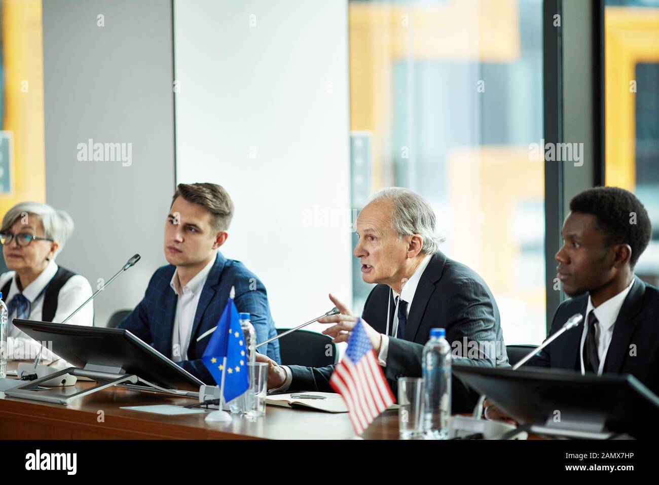 Senior man speaking the speech while sitting at the table among his ...