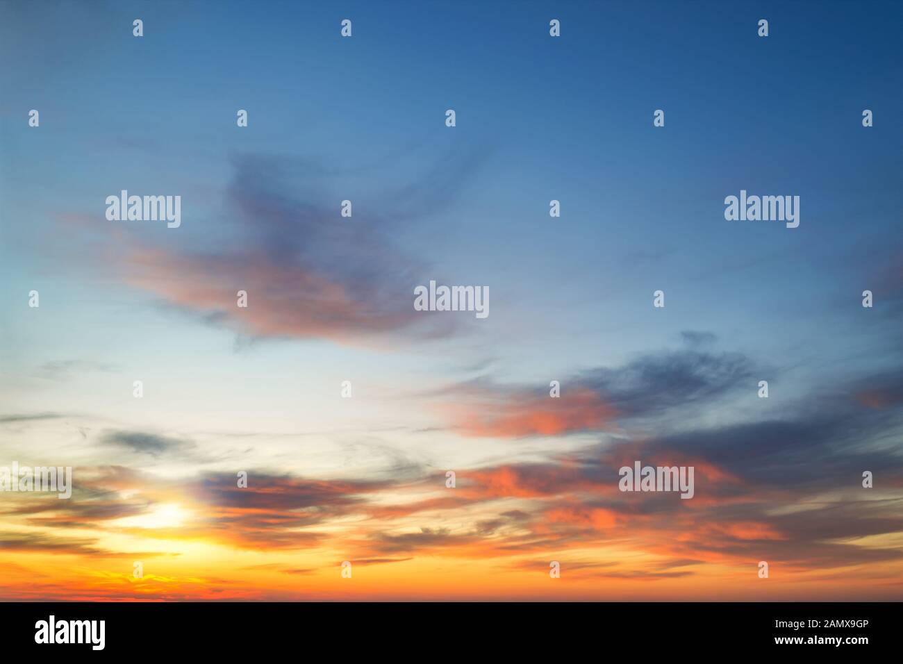 The setting sun shines through light clouds and paintes them with ...