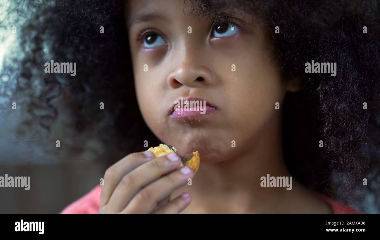Adorable mulatto curly girl eating cookie at home, child snacking close ...