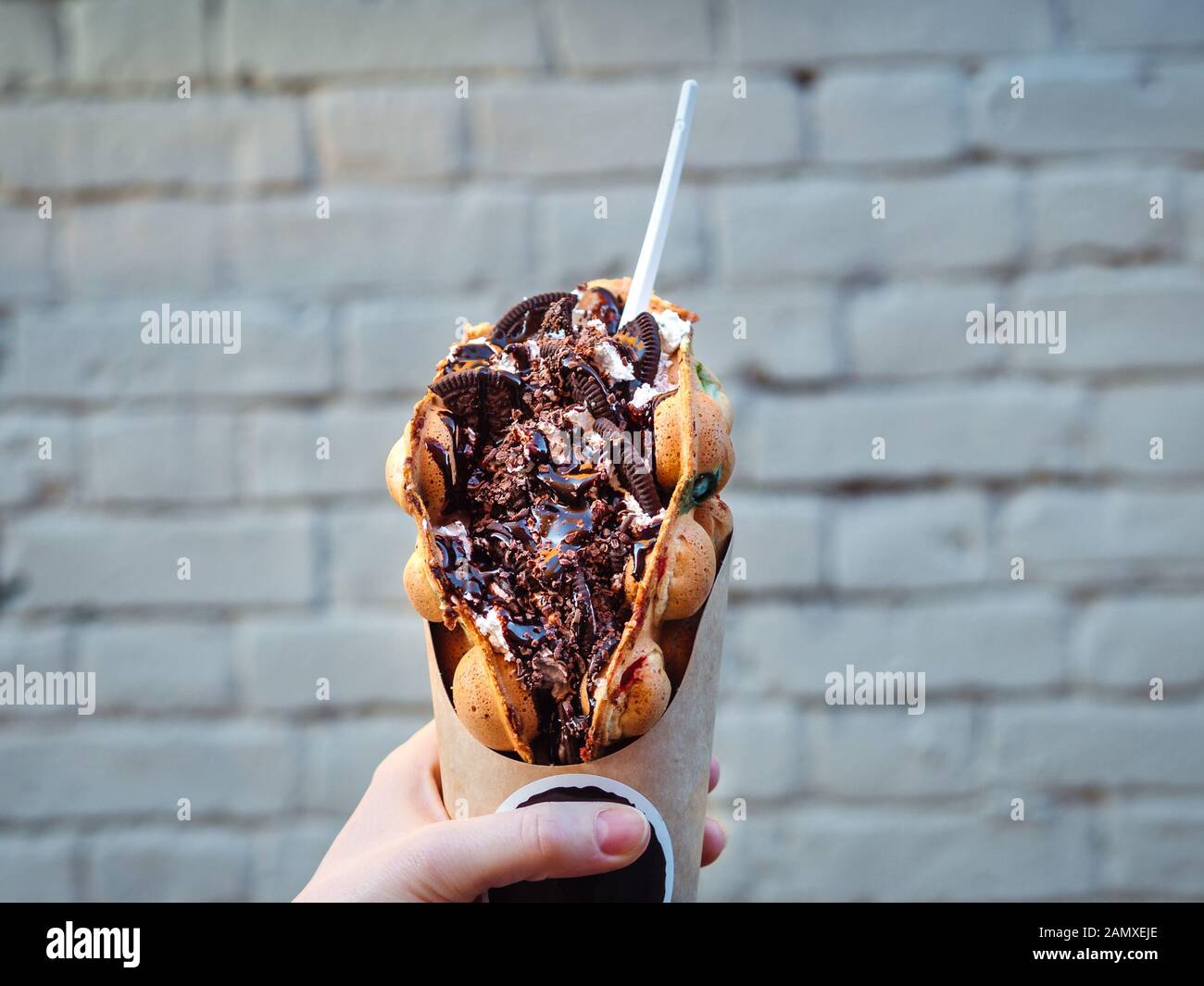 Hong Kong waffles in female hand on brick wall background. Delicious ...