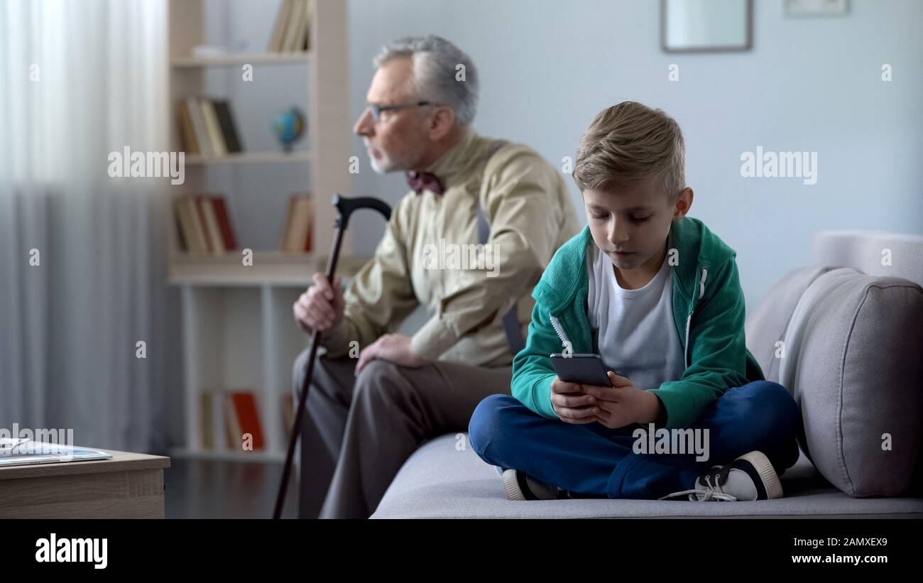 Boy using mobile phone, upset granddad sitting aside, internet ...